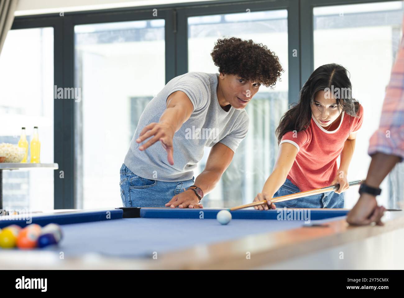 Playing pool, diverse friends aiming and focusing on billiard table ...