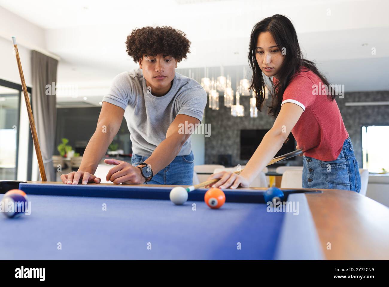 Playing pool, diverse friends focusing on making shots on billiards ...