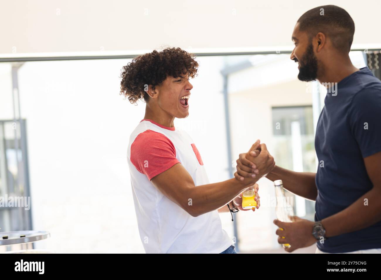 Diverse friends hanging out, two men shaking hands and holding drinks ...