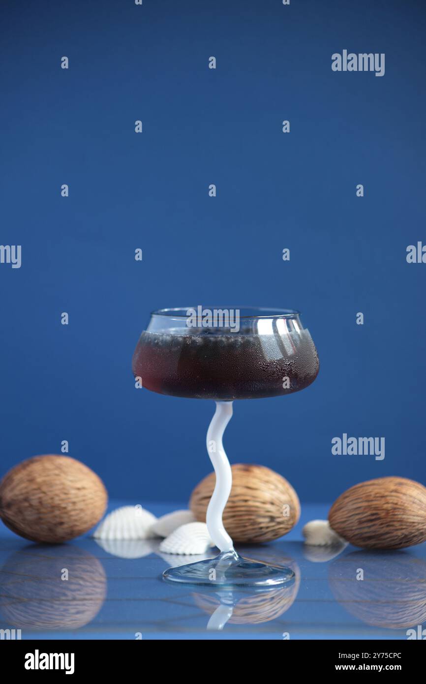 The burgundy cocktail in a glass with a white, flowing wavy stem ...