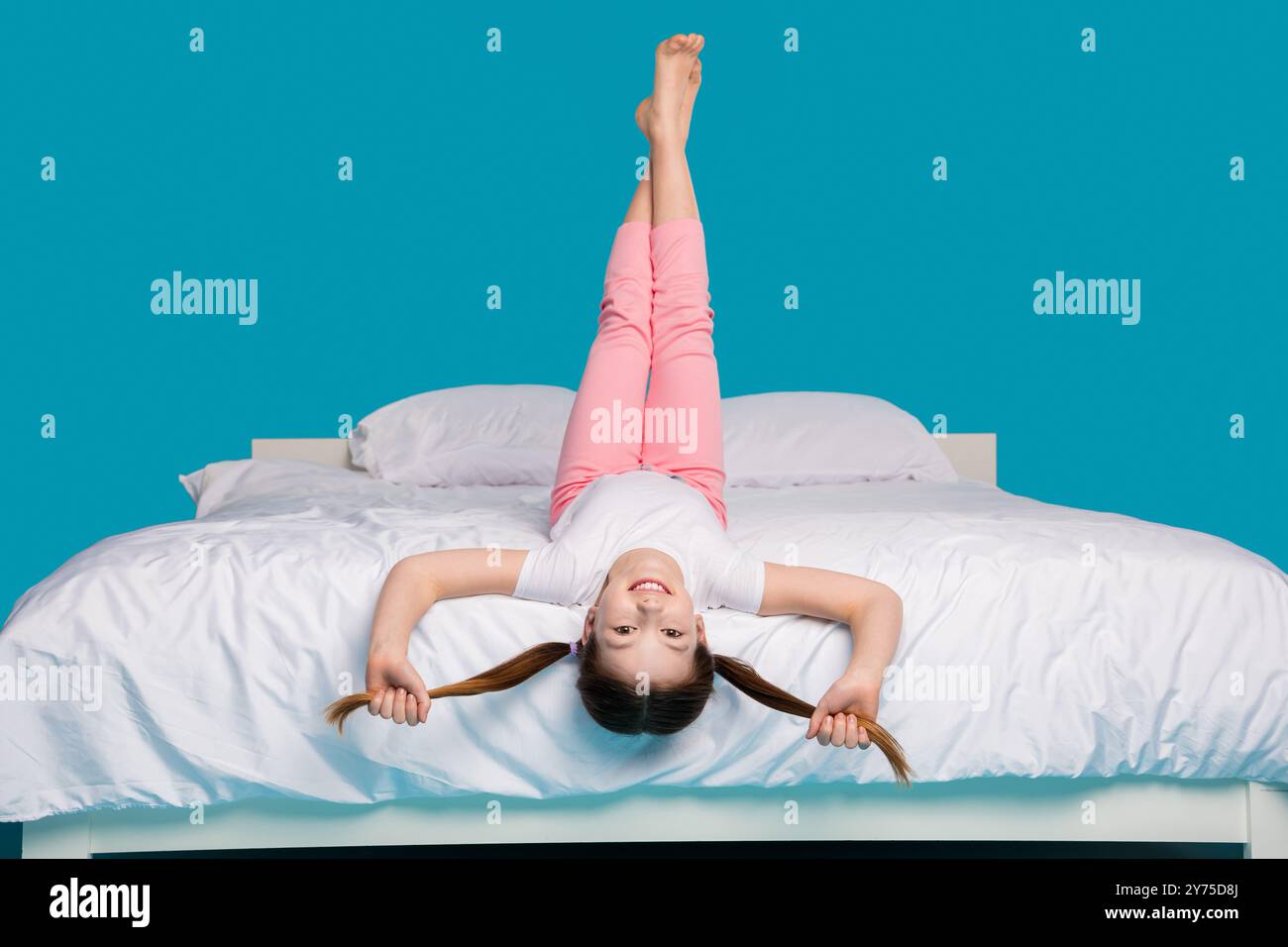 Full body photo of cute little girl pull tails upside down lying bed ...