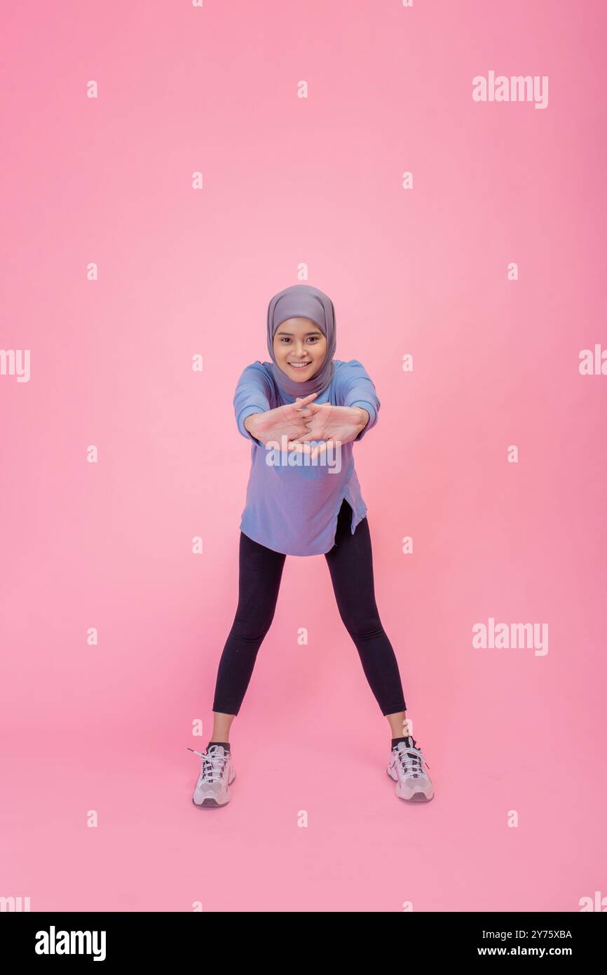 A woman in activewear stretches against a vibrant pink background to ...