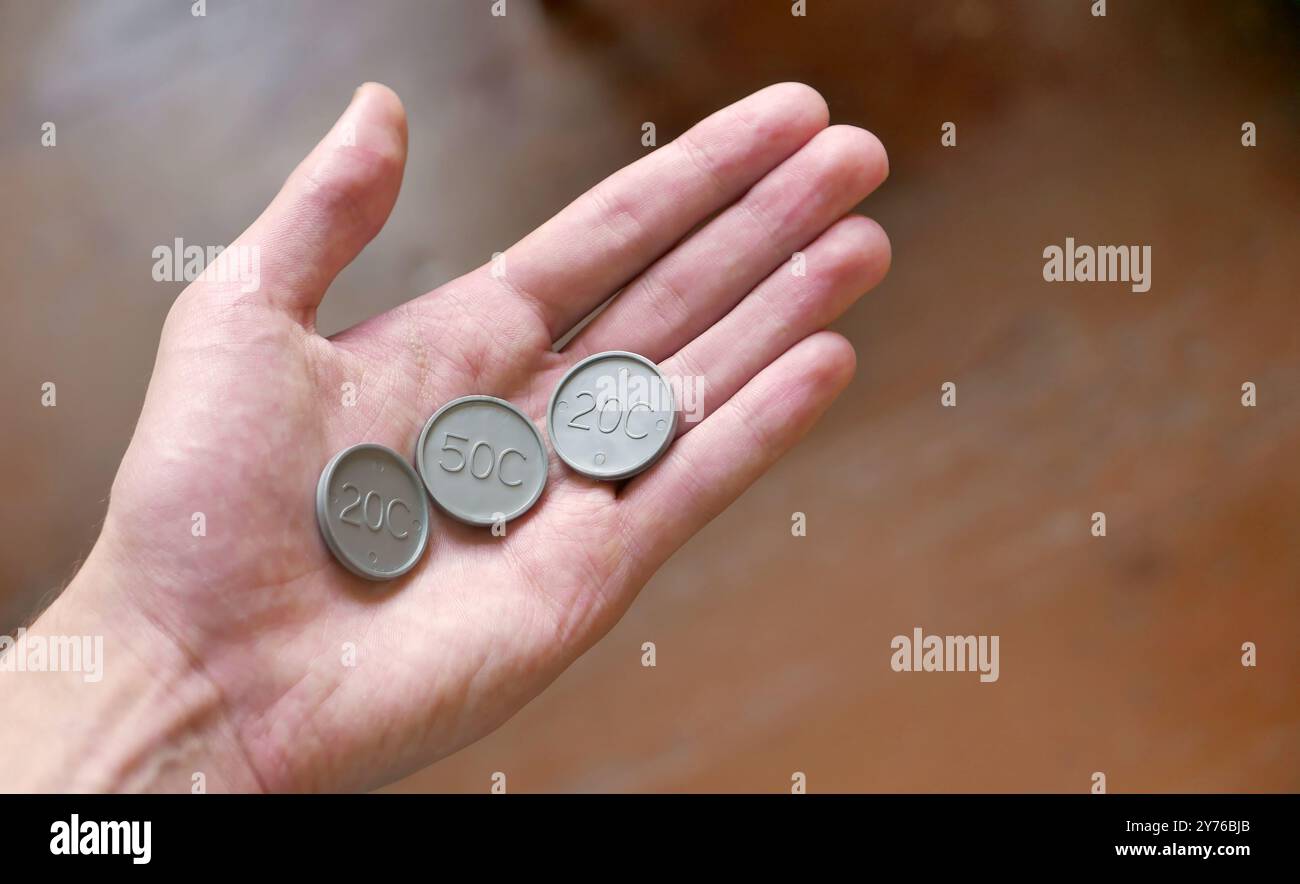 Hand holding out showing three fake grey toy plastic coins, currency ...