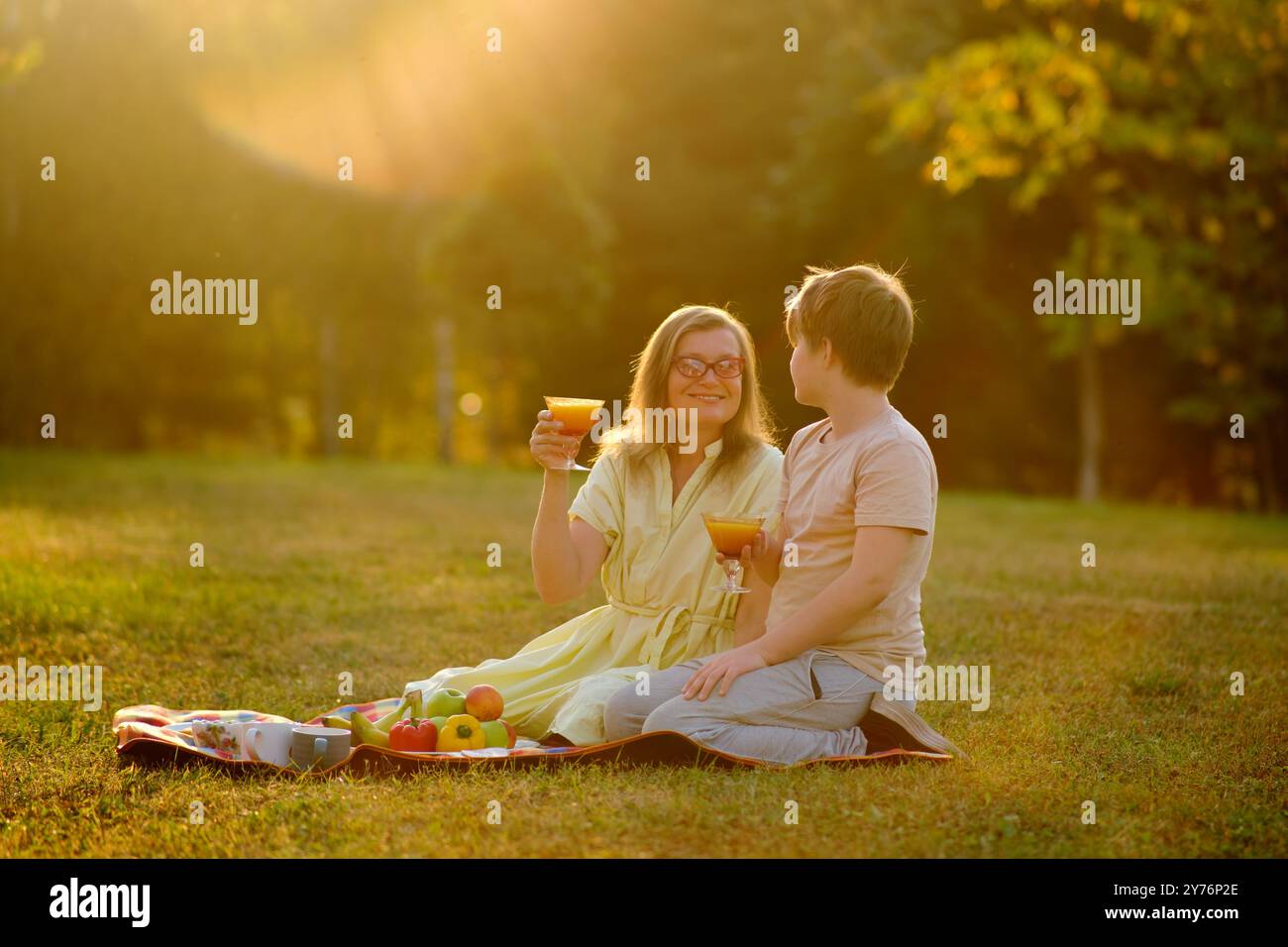 A cheerful woman and her teenage son were enjoying a picnic together in the summer sunshine. The ...