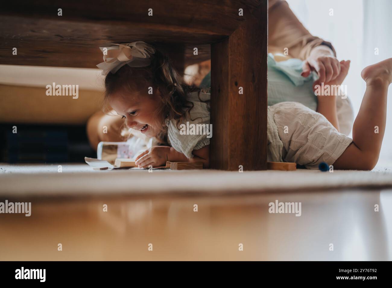 Joyful child playing under a table with caregiver holding hand Stock ...