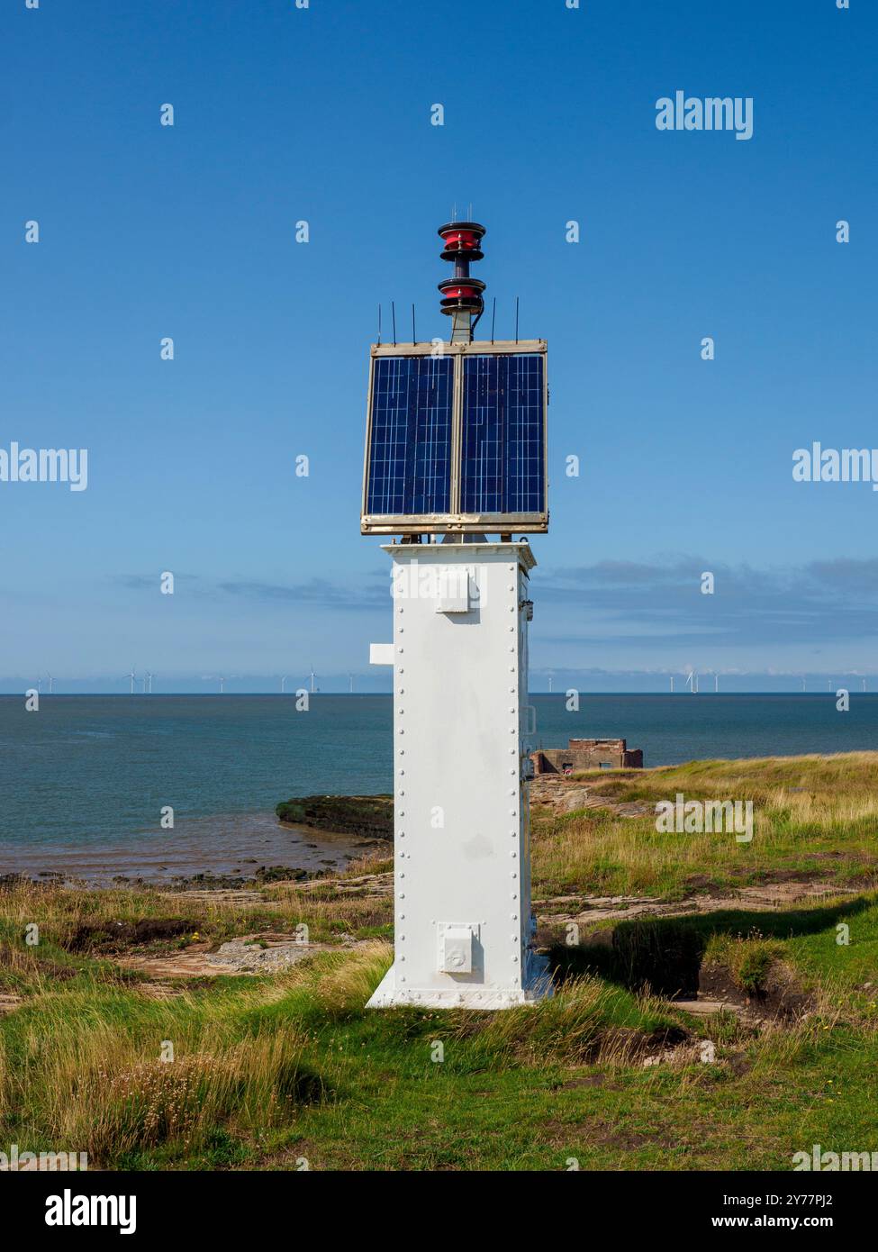 Solar-powered lighthouse standing tall by the sea under a clear blue ...
