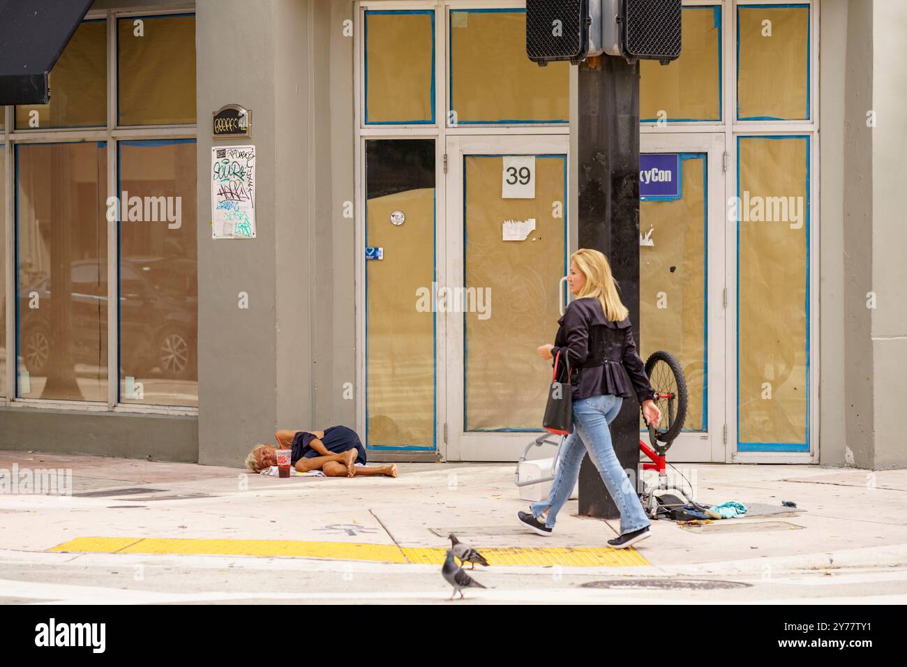 Miami, FL, USA - September 25, 2024: People walking by a homeless woman ...
