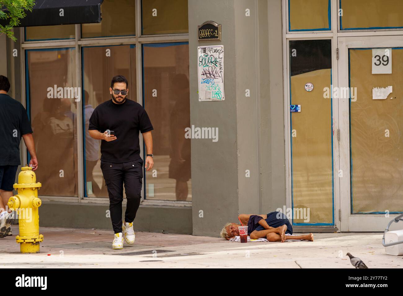 Miami, FL, USA - September 25, 2024: People walking by a homeless woman ...
