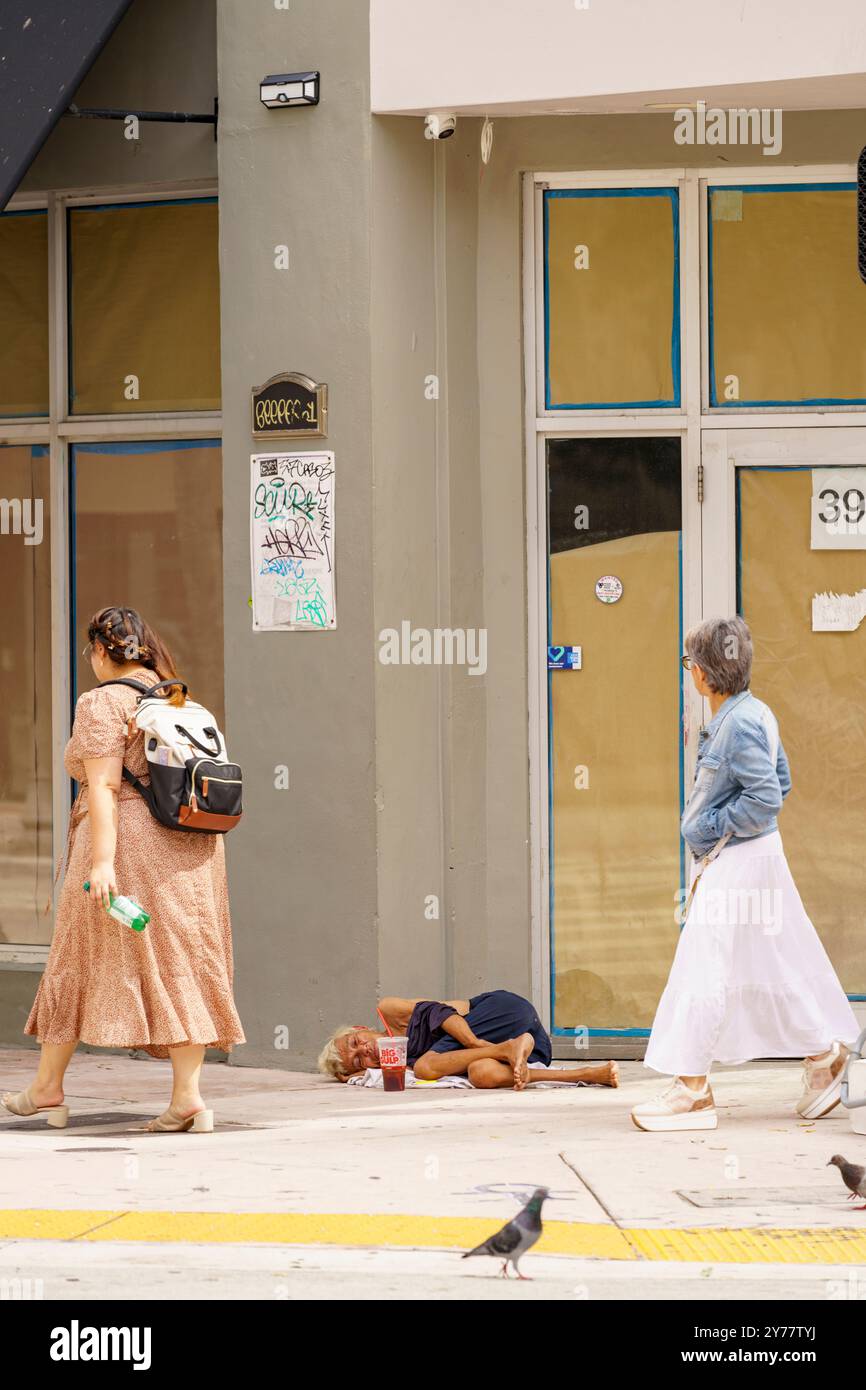 Miami, FL, USA - September 25, 2024: People walking by a homeless woman ...