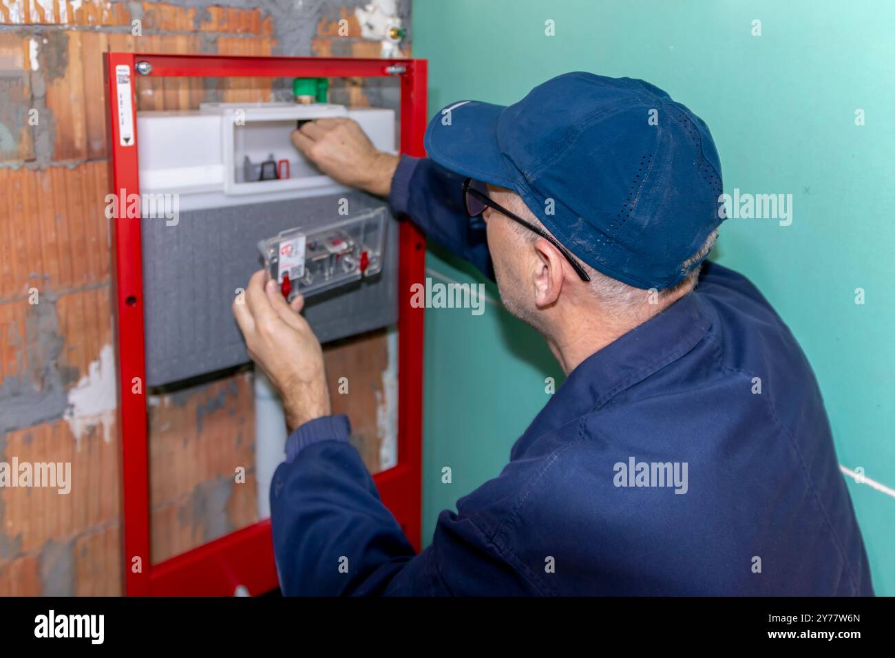 A mature experienced plumber installing the frame of a wall-mounted ...