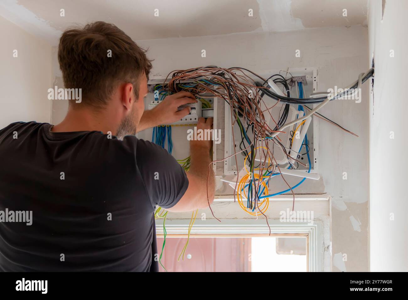 A male electrician works in a switchboard with an electrical connecting ...
