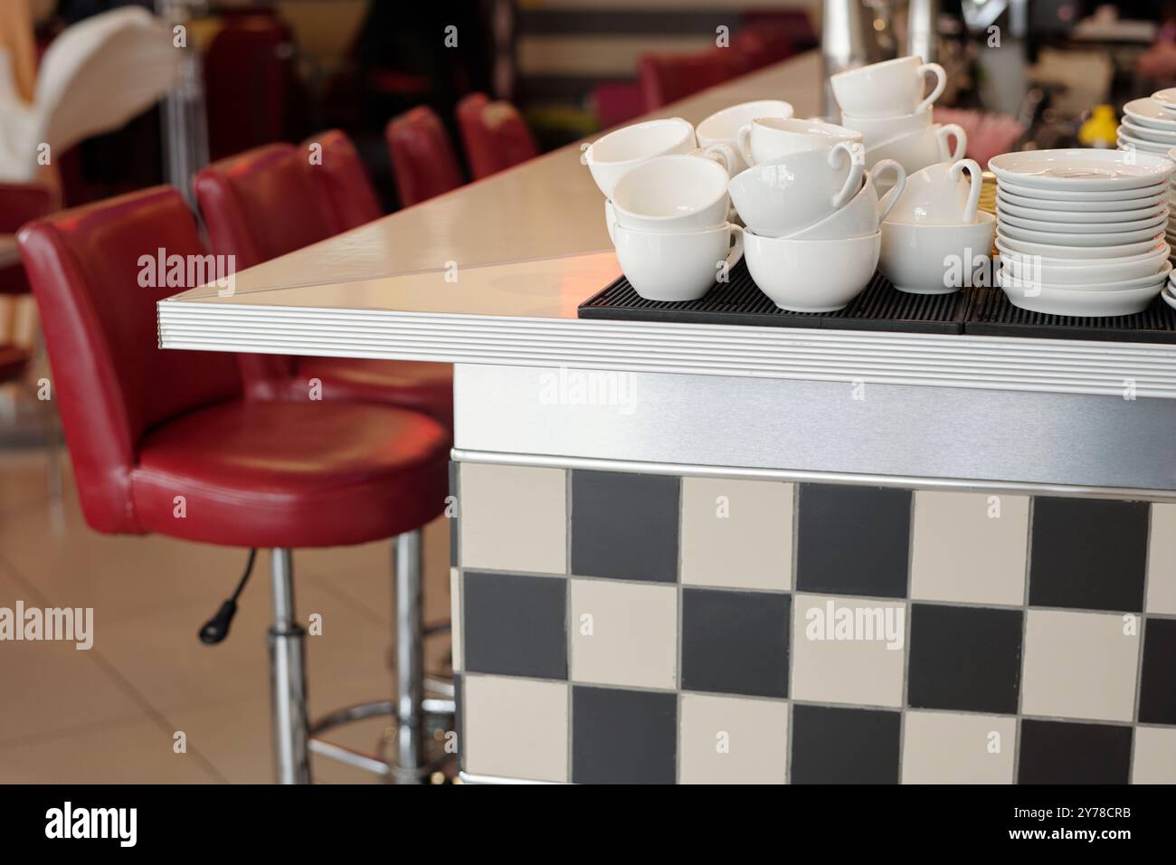 Grouping white cups neatly on counter near red bar stools in modern ...