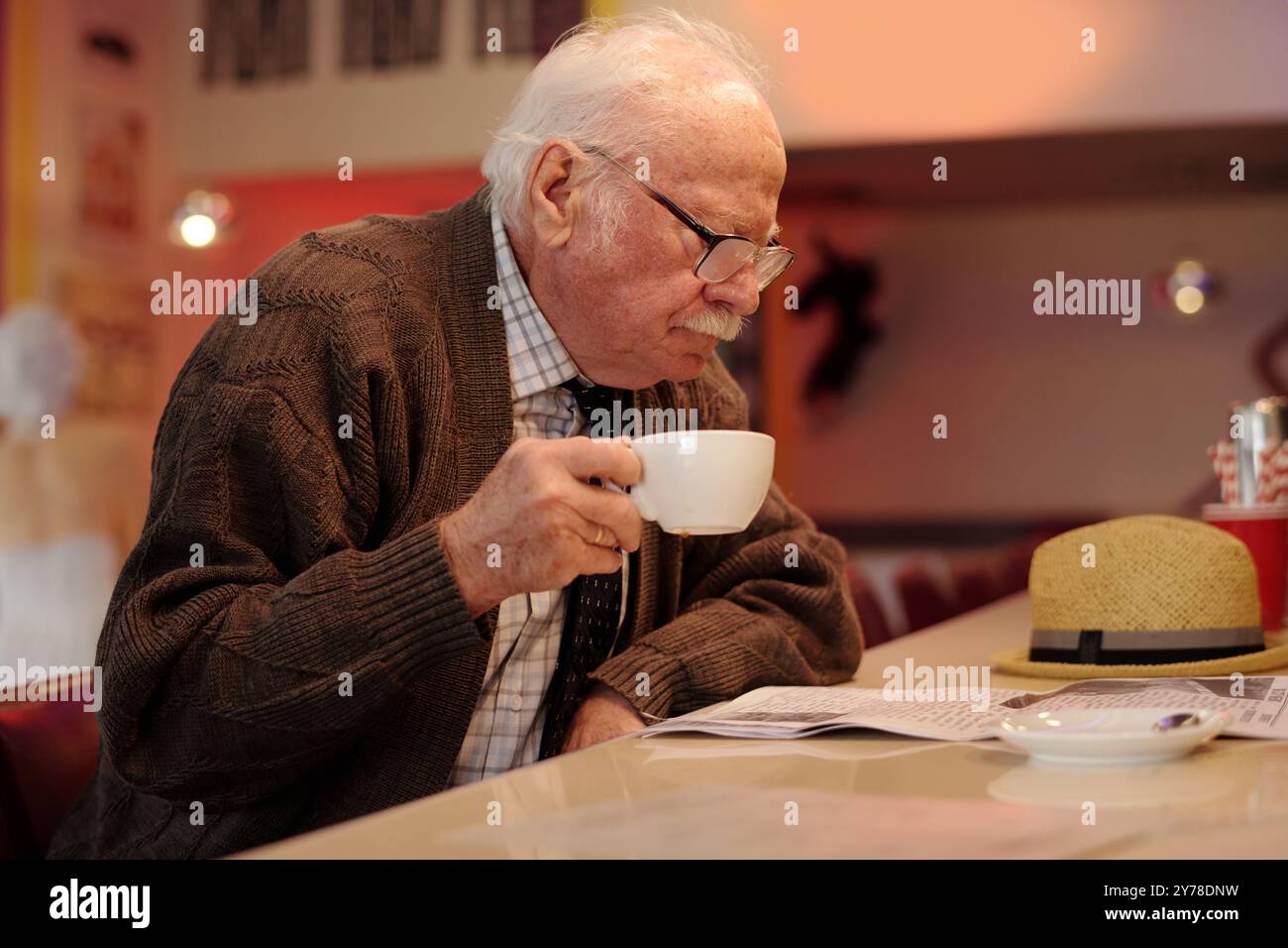 Senior man drinking coffee while reading newspaper in cozy cafe with ...