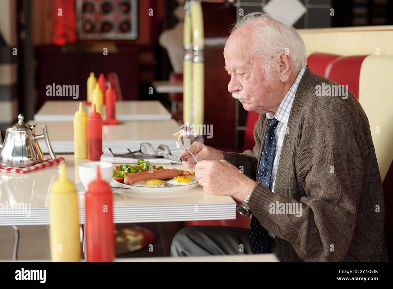 Senior man eating meal in classic diner featuring retro decor and ...