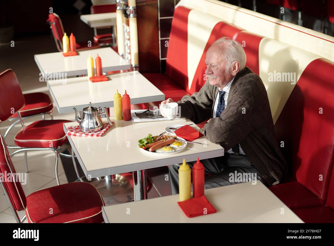 Elderly man enjoying breakfast in classic American diner with red ...