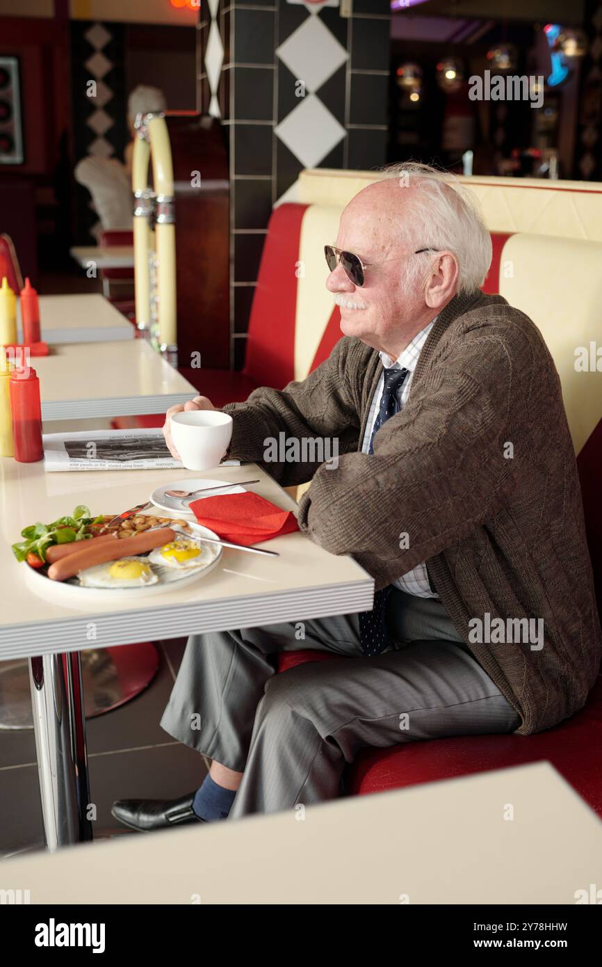 Elderly man sitting in retro diner booth, enjoying breakfast with eggs ...