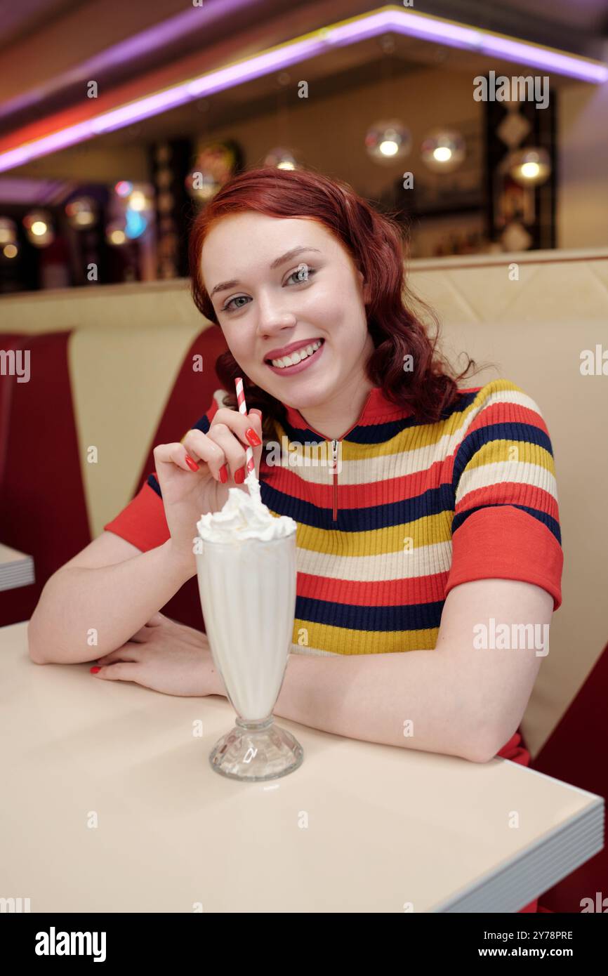 Portrait of young Caucasian woman with red hair holding and sipping a ...