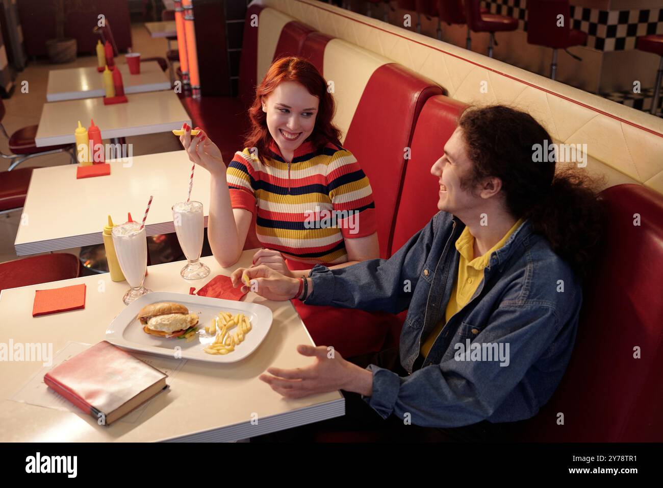 Young couple smiling and enjoying their meal in a retro diner booth ...
