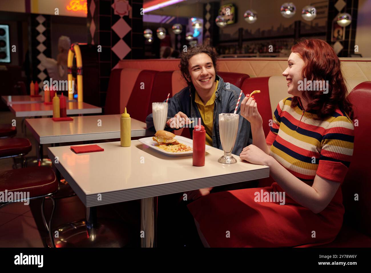 Two friends are enjoying milkshakes and burgers in a classic American ...