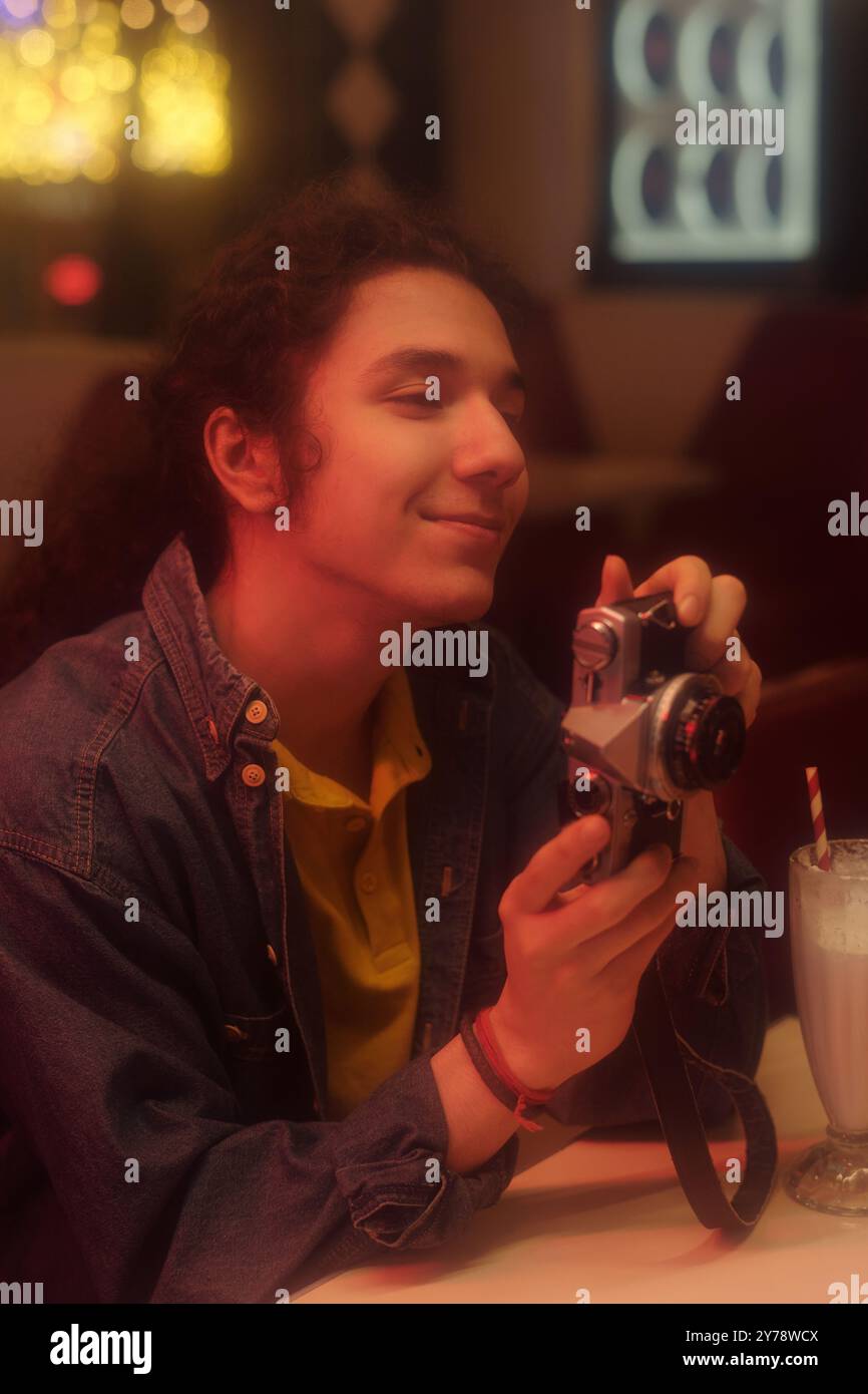 Young man sitting at table while holding vintage camera and enjoying ...