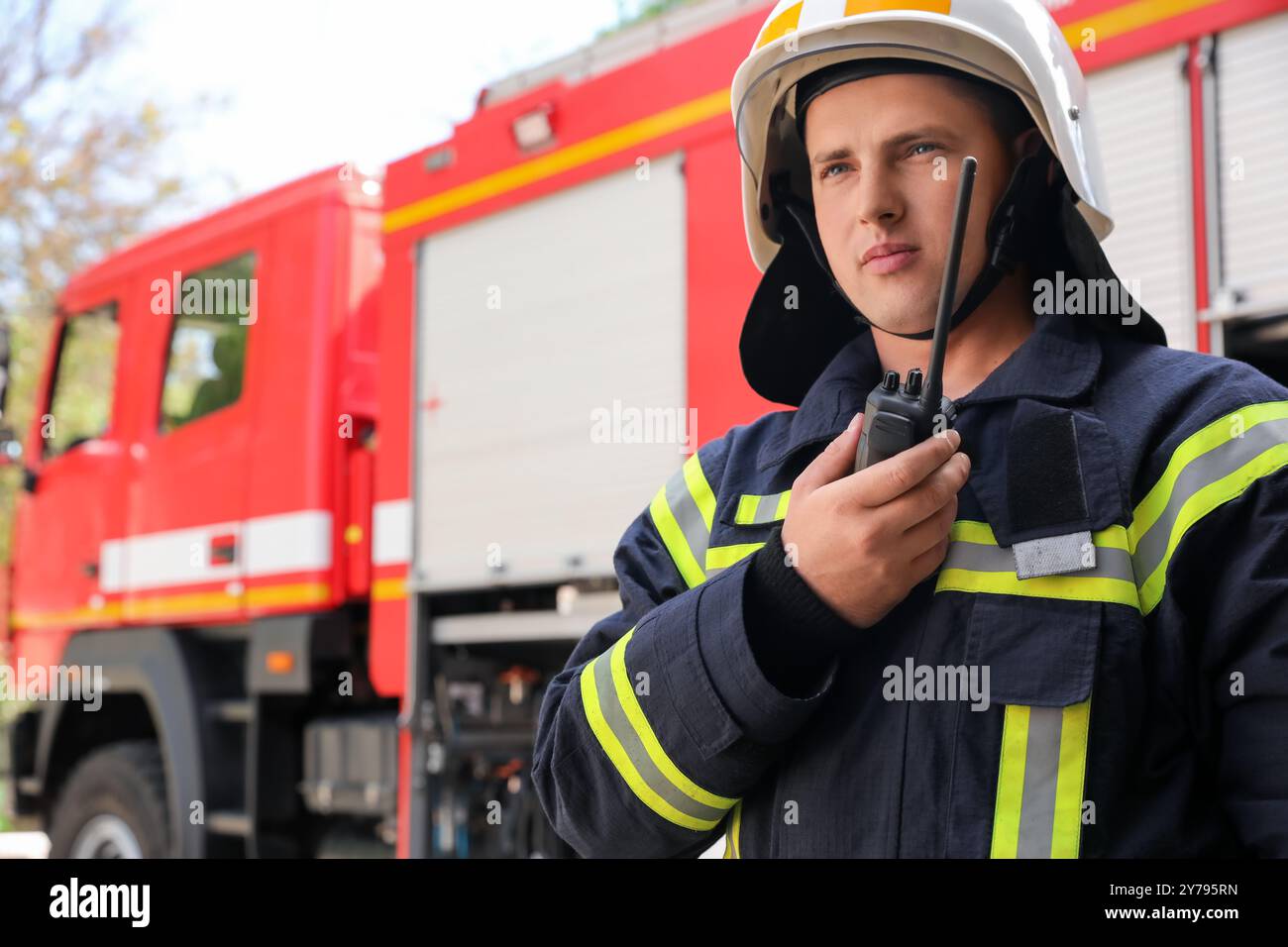 Portrait of firefighter in uniform with portable radio set near fire ...
