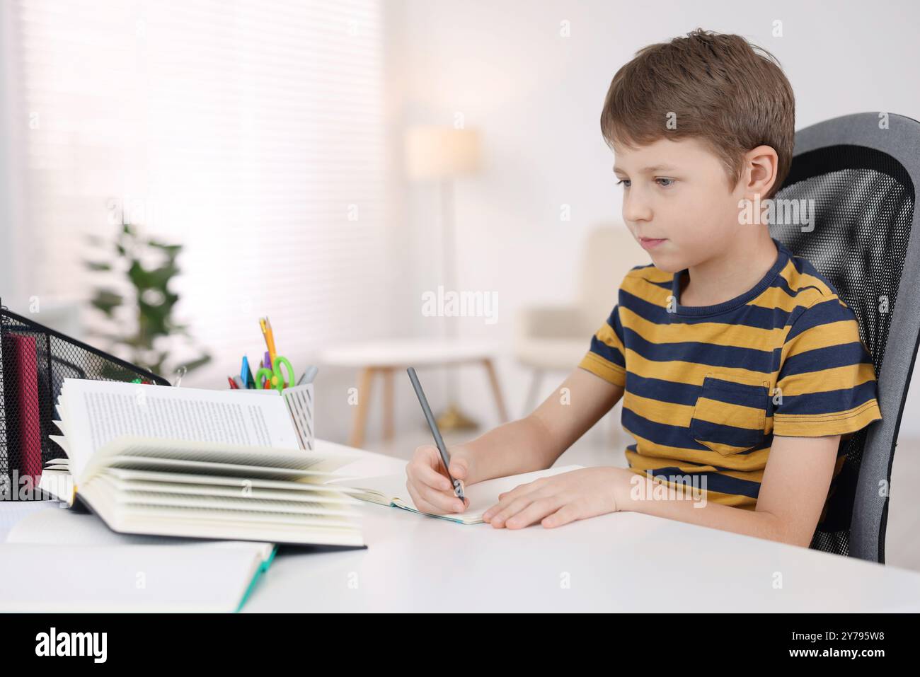 Boy with correct posture doing homework at white desk indoors Stock ...