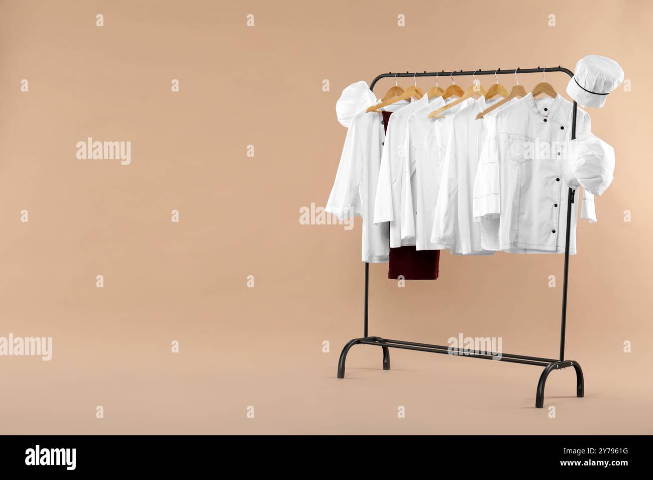 Different chef's uniforms on clothing rack against beige background ...