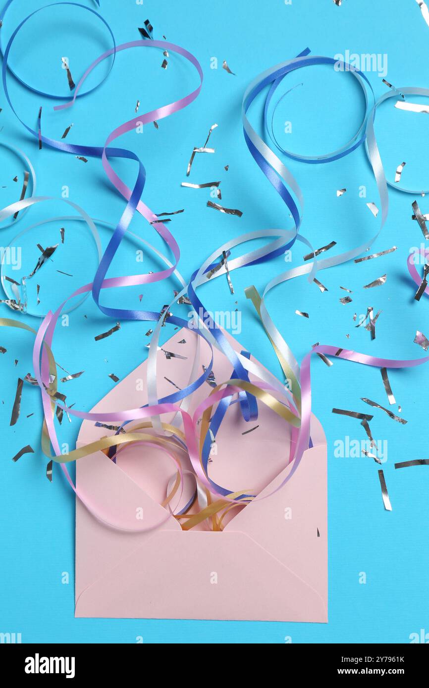 Shiny confetti and party streamers flying out of envelope on light blue ...