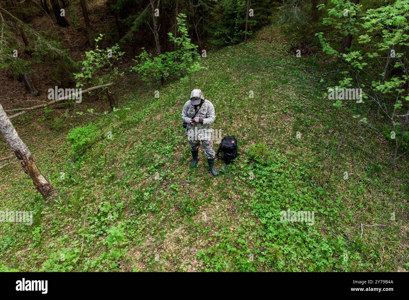 A man in camouflage among trees looks at the screen of the drone ...