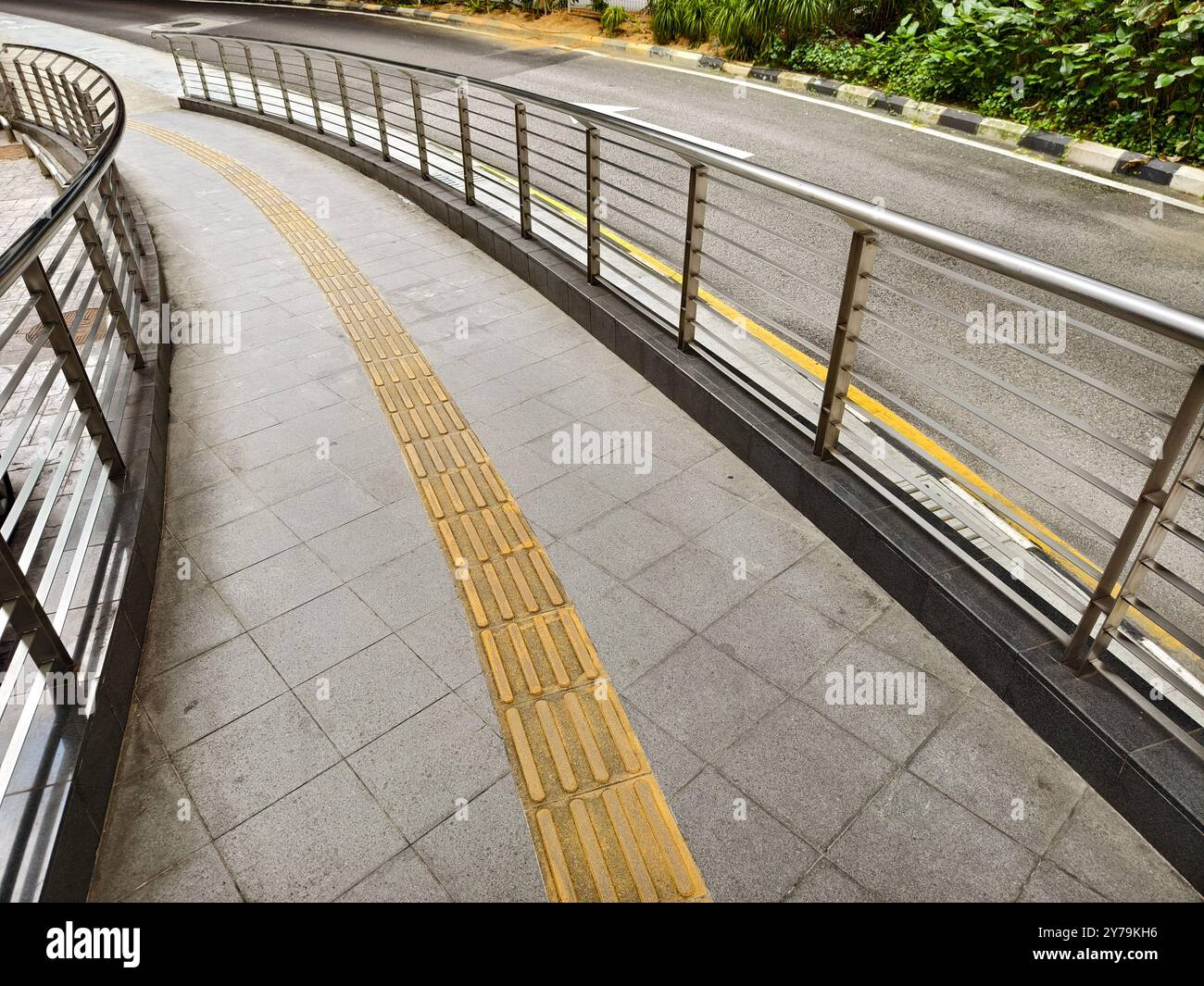 Curved path with guardrail and yellow line for blind people along the ...
