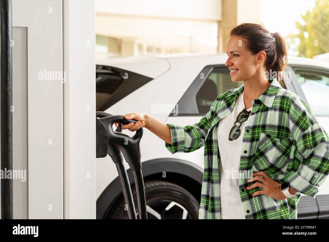 Woman at an EV charging station in the city, charging her electric car ...