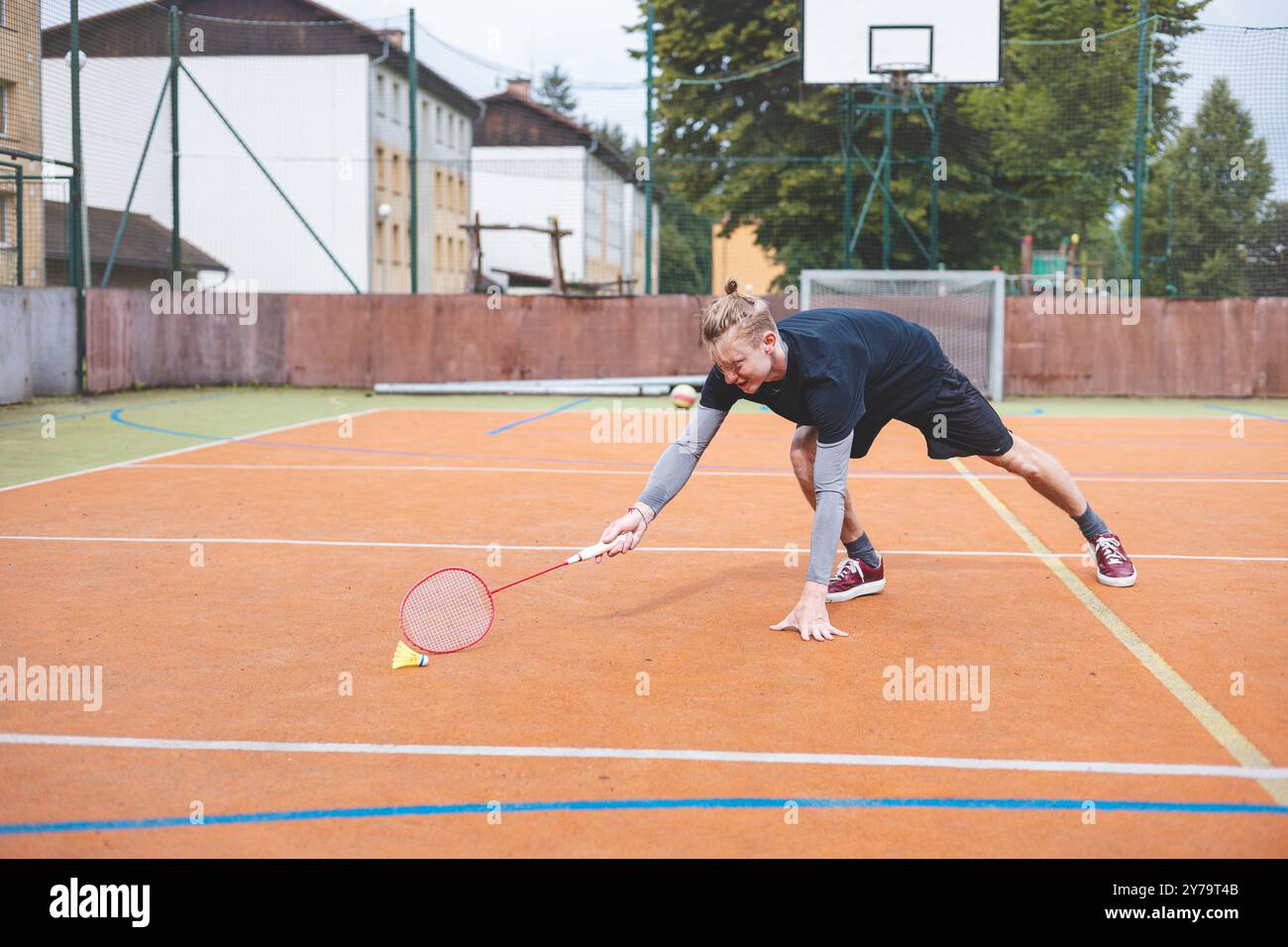 Badminton player stretches to retrieve a low shuttlecock during an ...