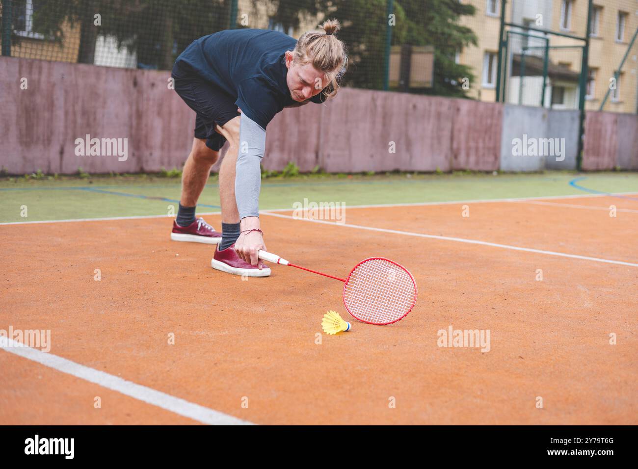 Badminton player stretches to retrieve a low shuttlecock during an ...