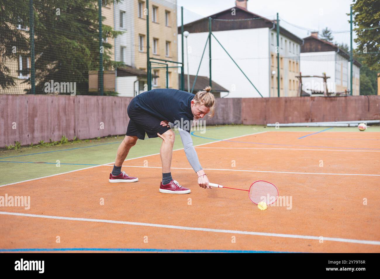 Badminton player stretches to retrieve a low shuttlecock during an ...