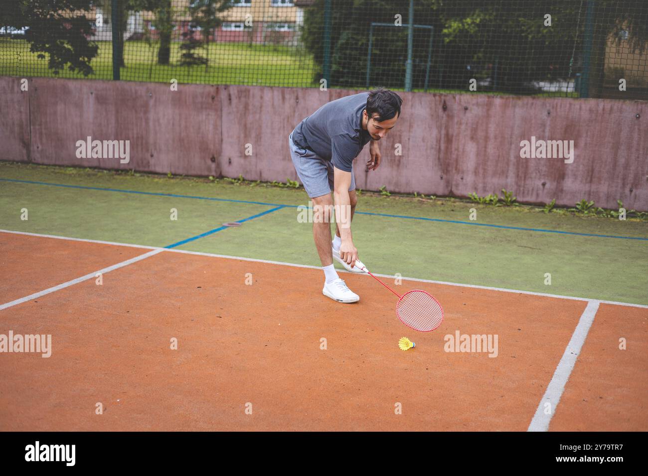 Badminton player stretches to retrieve a low shuttlecock during an ...