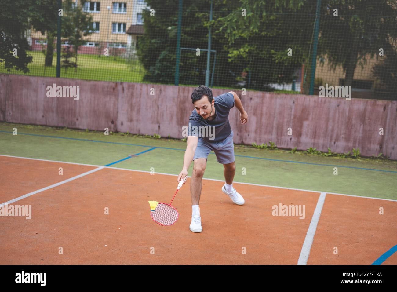 Badminton player stretches to retrieve a low shuttlecock during an ...