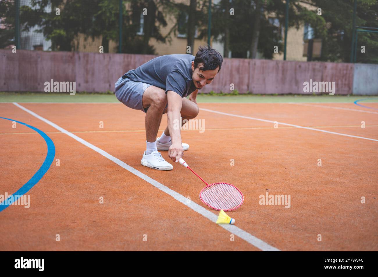 Badminton player stretches to retrieve a low shuttlecock during an ...