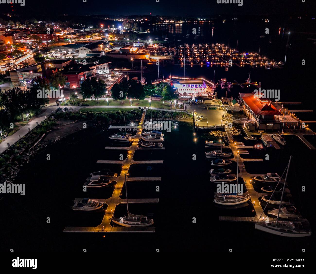 Aerial night view of a vibrant marina with boats docked and city lights ...