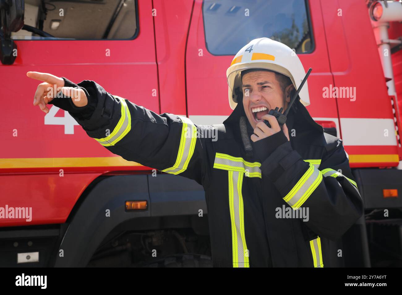 Firefighter in uniform using portable radio set near fire truck ...