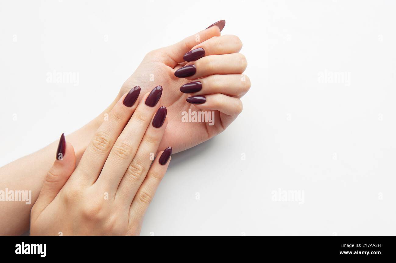 Two hands showcase a stylish deep burgundy nail design on a stark white ...