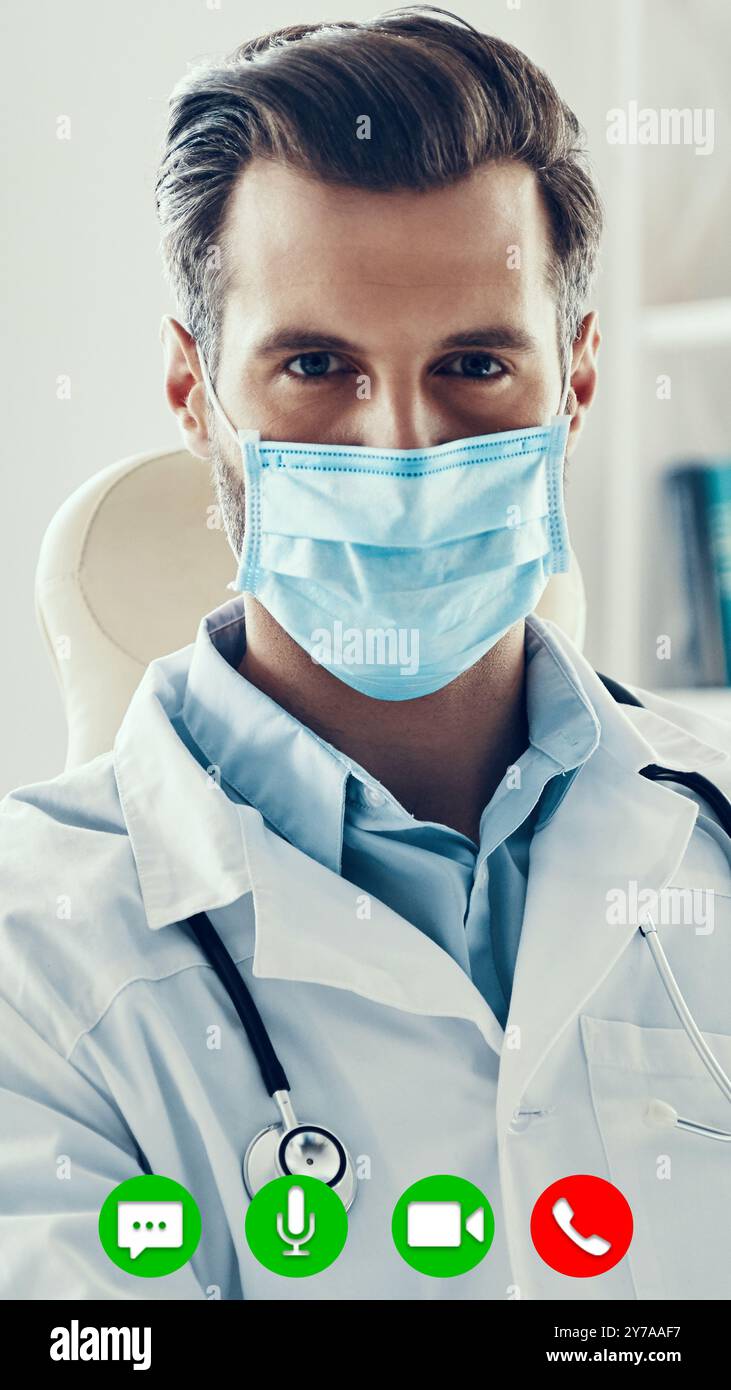 Serious young man in white lab coat and protective mask looking at ...