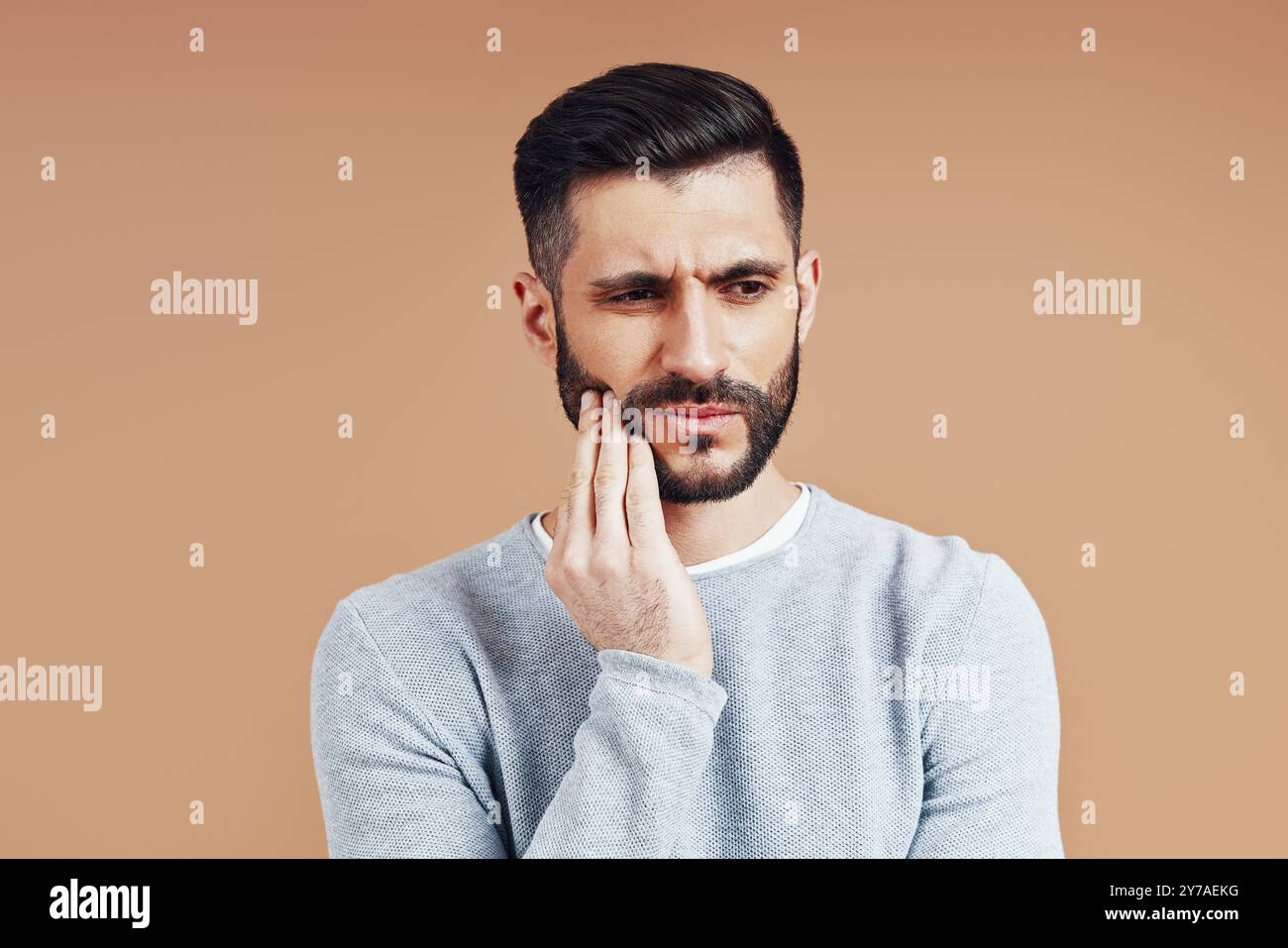 Frustrated young man in smart casual wear holding hand on cheek while ...