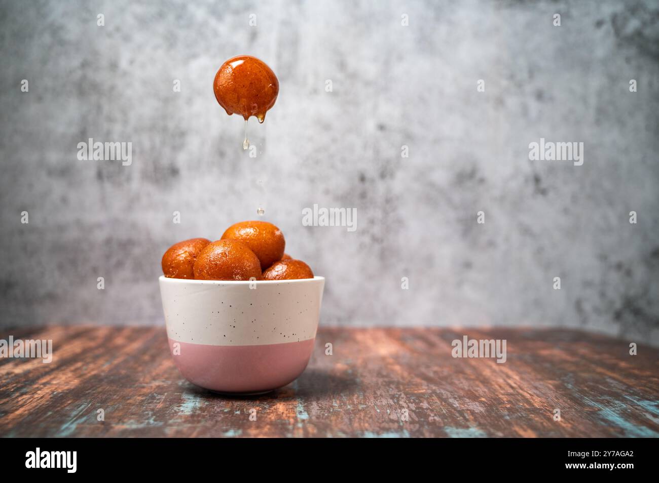 Gulab Jamun served in a bowl with pouring sweet syrup. Gulab Jamun is a ...