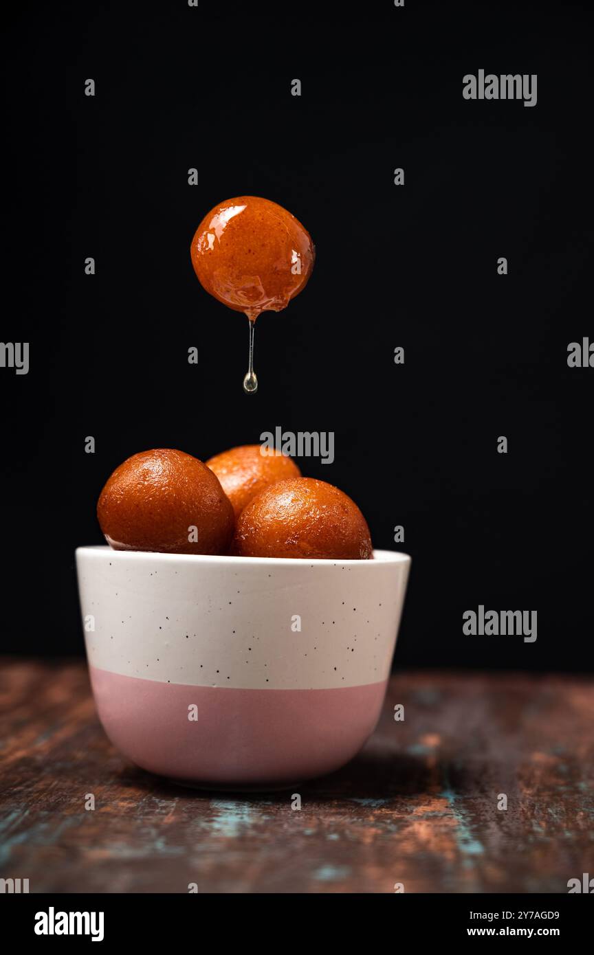 Gulab Jamun served in a bowl with pouring sweet syrup. Gulab Jamun is a ...