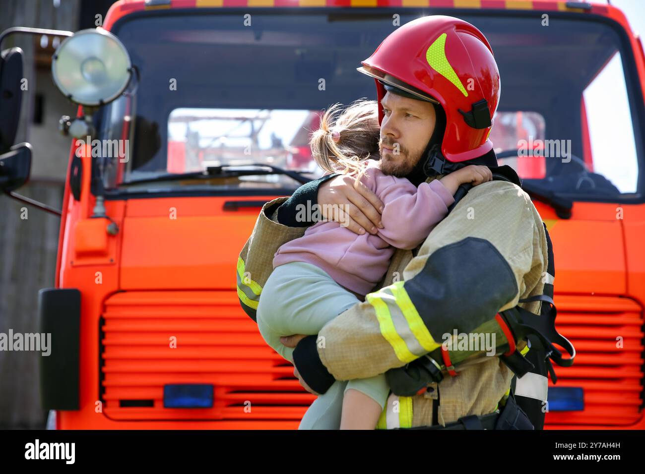 Firefighter in uniform holding rescued little girl near fire truck ...