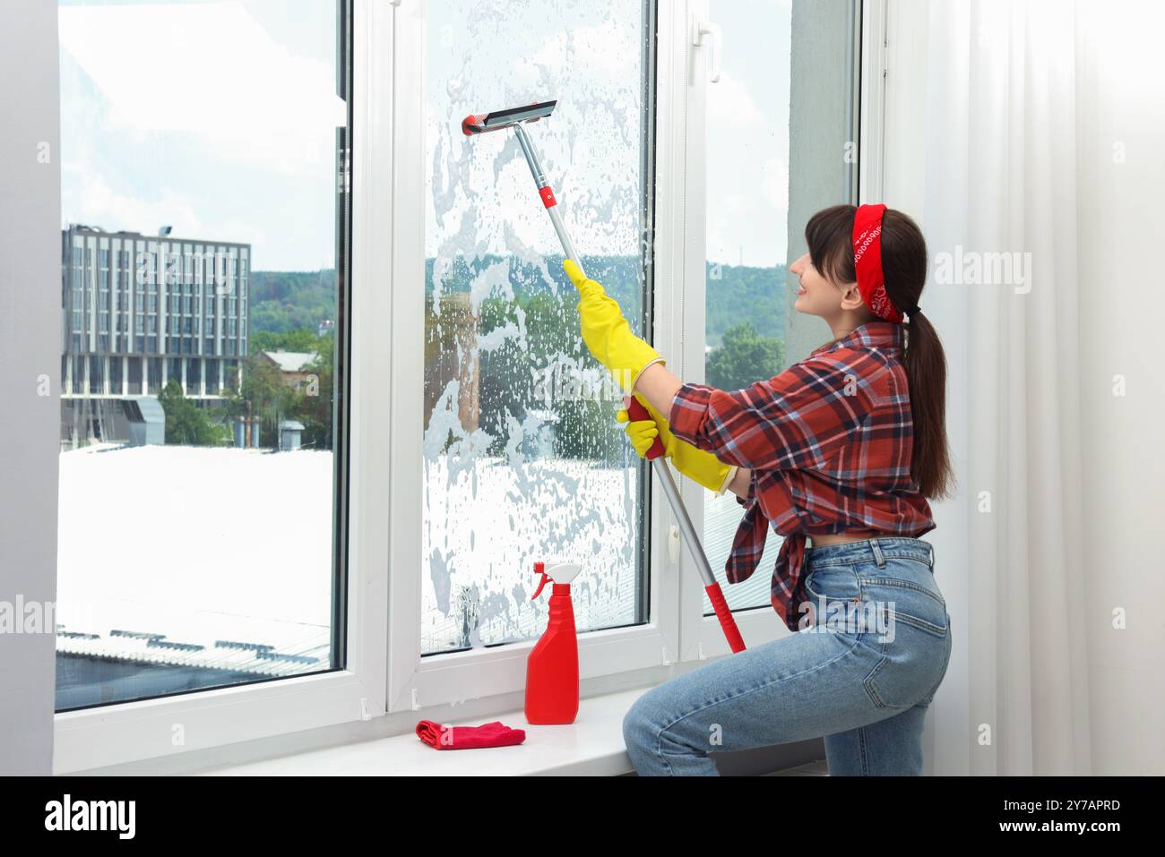 Young woman with squeegee tool cleaning window indoors Stock Photo - Alamy