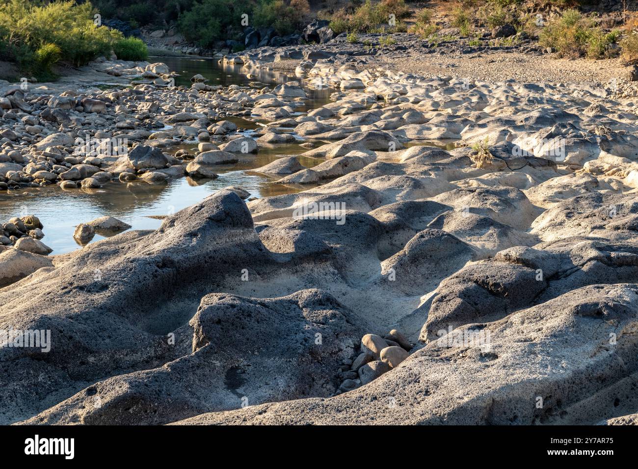 Smooth water-worn stones and ancient volcanic rocks form the bed of the ...