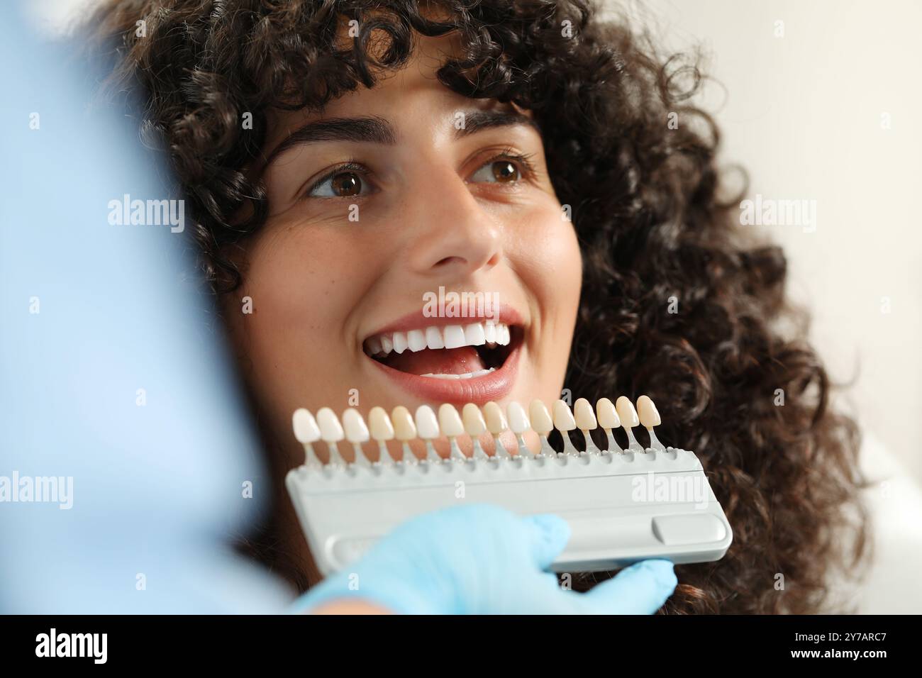 Doctor checking young woman's teeth color in clinic, closeup. Dental ...