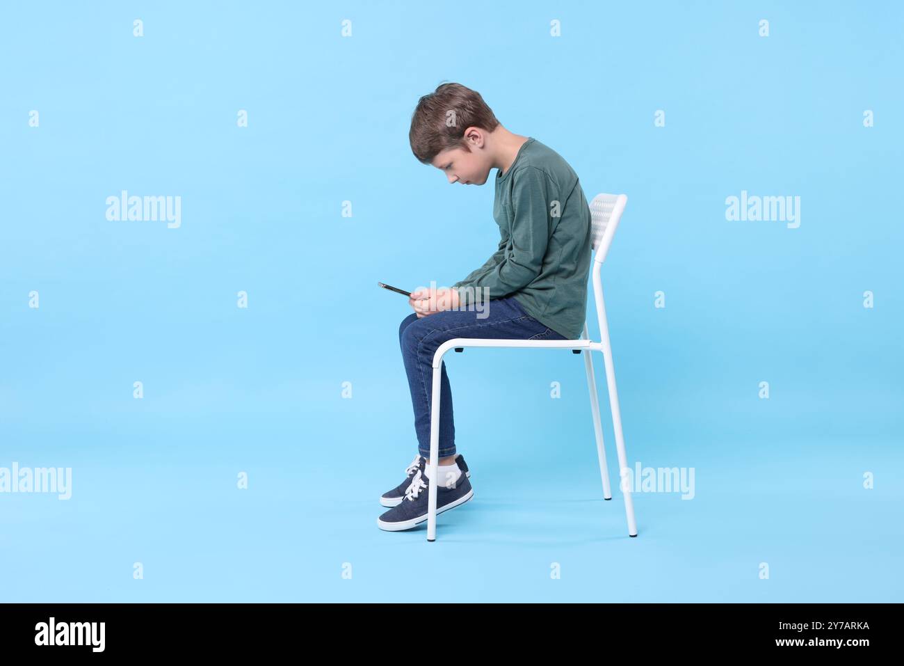 Boy with incorrect posture and phone sitting on chair against light ...