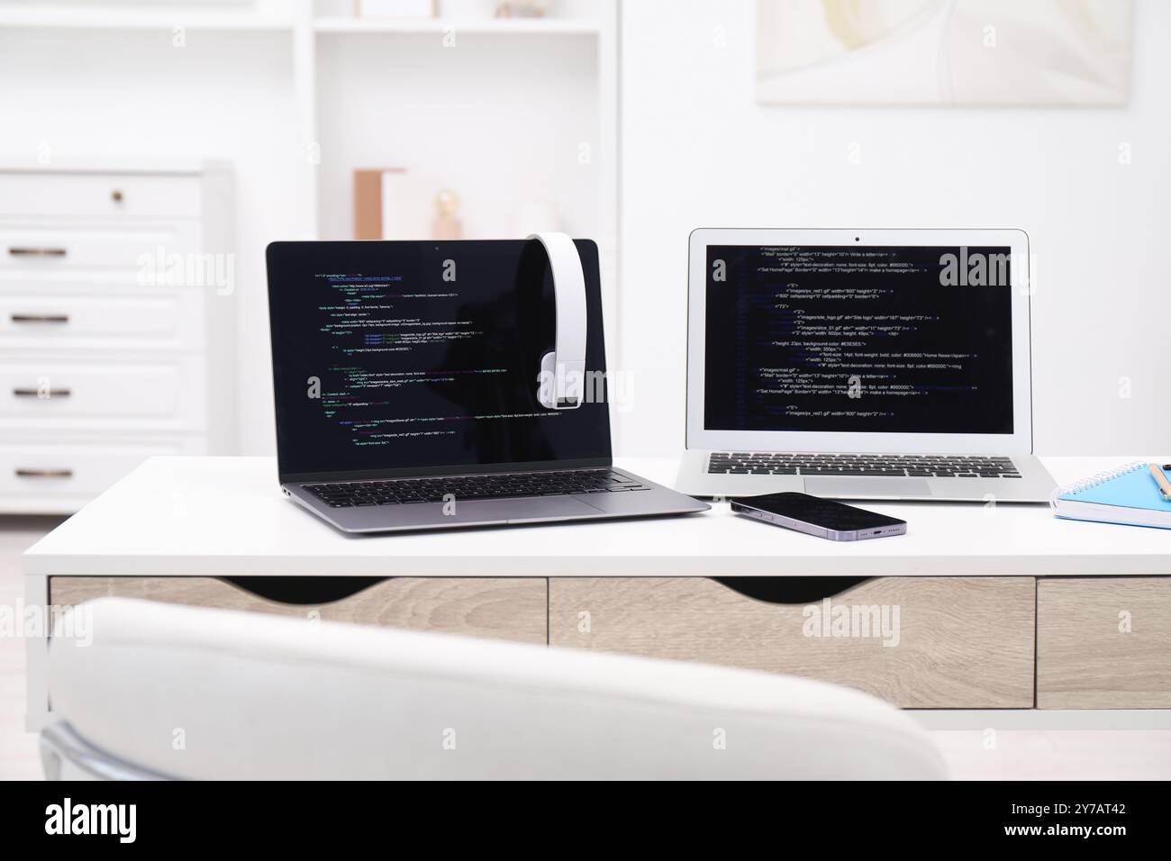 Programmer's workplace. Modern laptops with unfinished code, headphones and smartphone on desk ...
